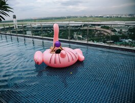 Uma pessoa flutua em um piscinão rosa com vista para a cidade.