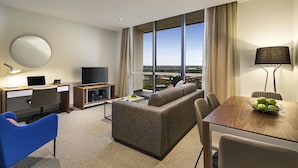 Quarto de hotel moderno com sofá, mesa de jantar, televisão e uma grande janela com vista para a cidade.
