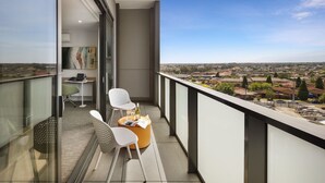 Uma varanda com vista desobstruída da cidade, uma área de estar pequena com cadeiras e uma mesa, e um quadro na parede.