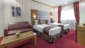 Quarto de hotel com duas camas, um sofá, uma mesa de madeira e um quadro na parede.