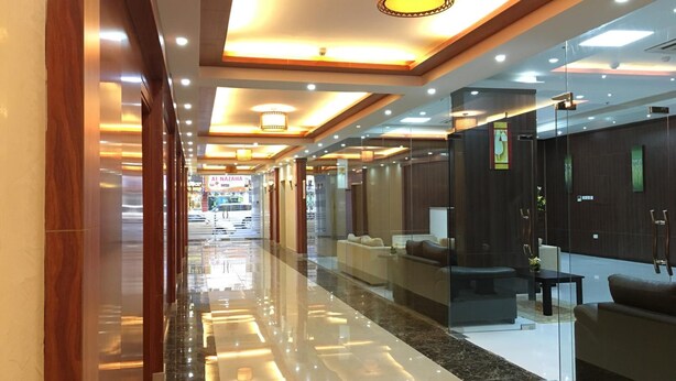 Um hall de hotel moderno com piso de mármore refletivo, divisórias de vidro e uma área de estar com sofás.
