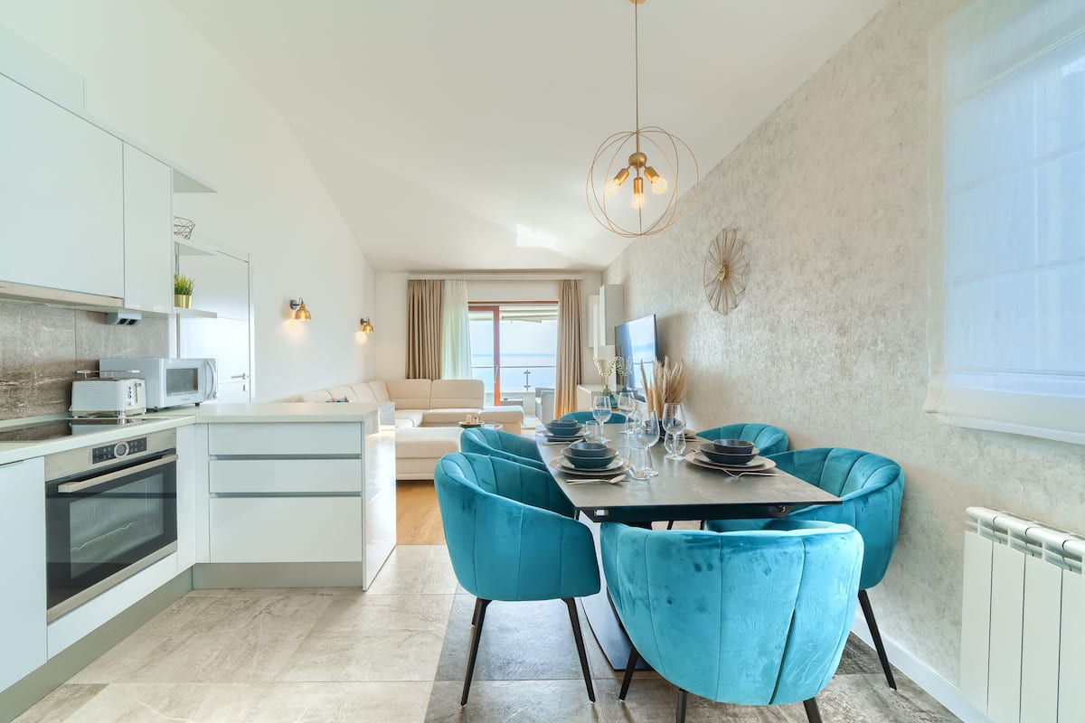 Cozinha moderna com armários brancos, micro-ondas e área de jantar com cadeiras azul-turquesa e mesa posta para dois.