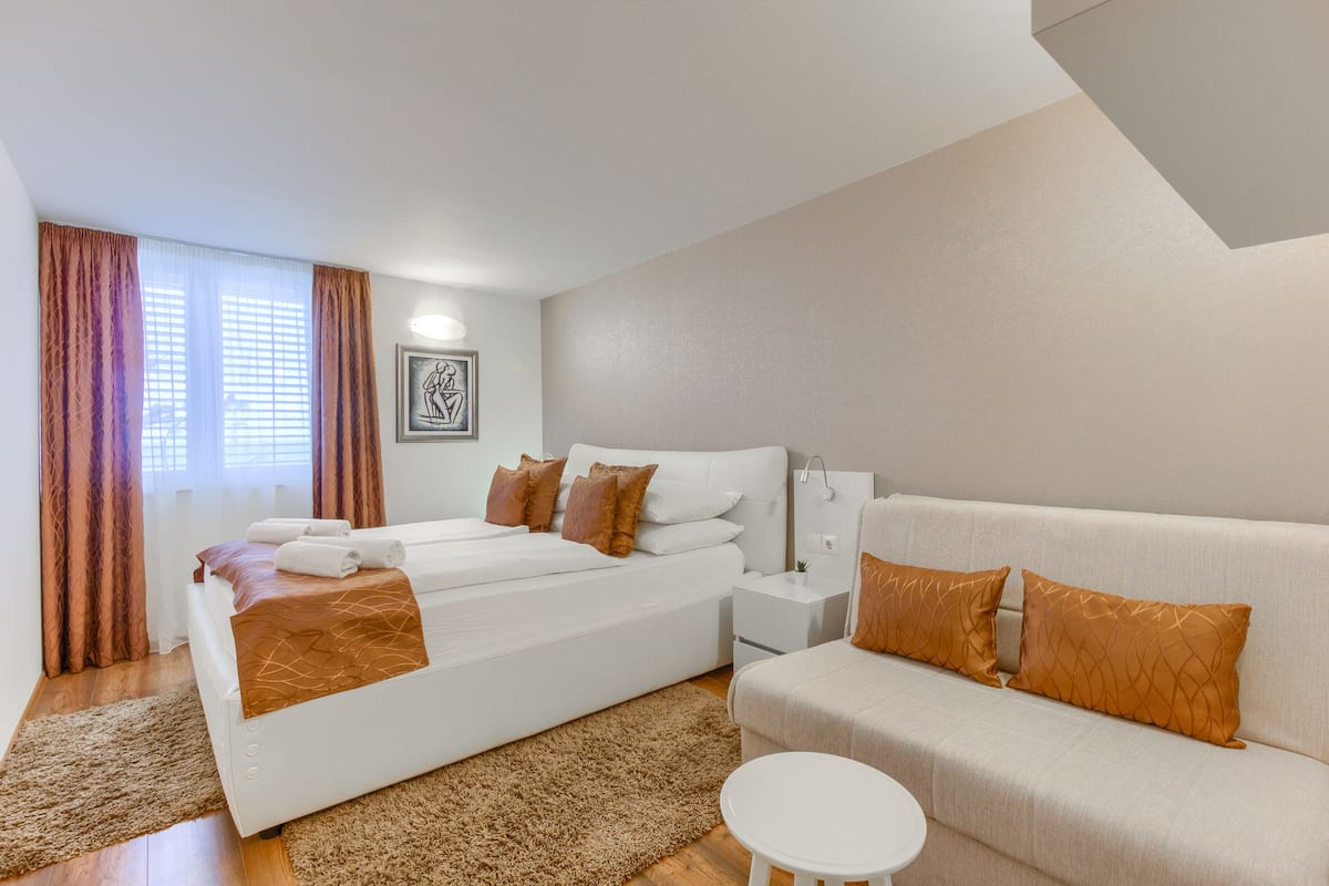 Quarto de hotel moderno com uma cama grande, um sofá, uma mesa pequena e uma mesinha de cabeceira.