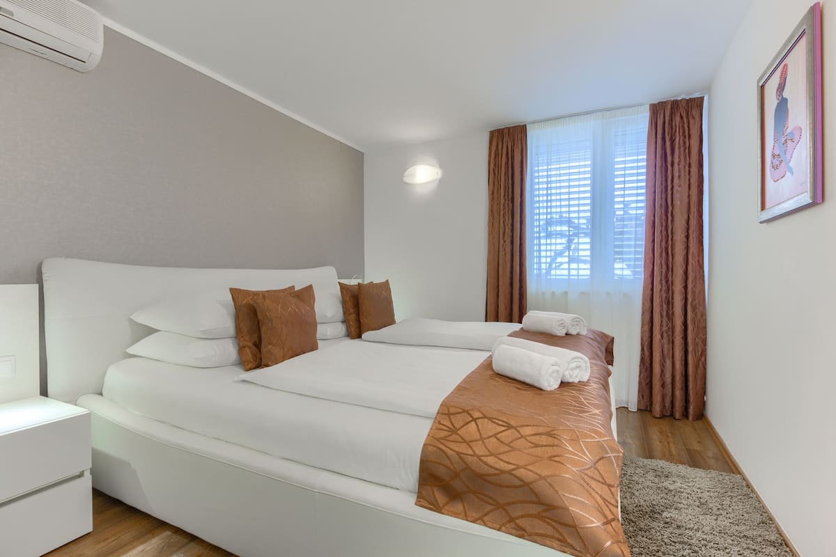 Quarto de hotel com cama grande, mesa de cabeceira, cortinas numa janela e um quadro na parede.