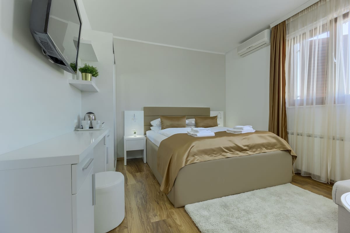 Quarto de hotel moderno com cama, mesa de cabeceira e televisão na parede.