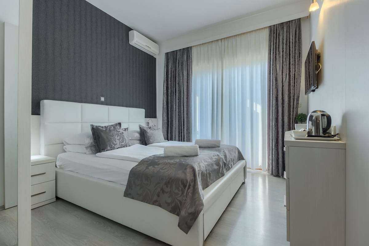 Quarto moderno com cama grande, mesas de cabeceira, televisão integrada e pequena área de kitchenette.