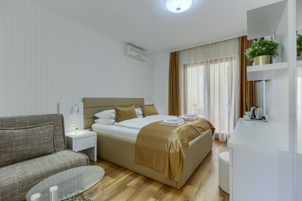 Quarto de hotel moderno com uma cama, um sofá, uma mesinha e uma cozinha compacta.