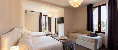 Quarto de hotel com duas camas, um sofá, uma televisão e uma janela grande com cortinas.