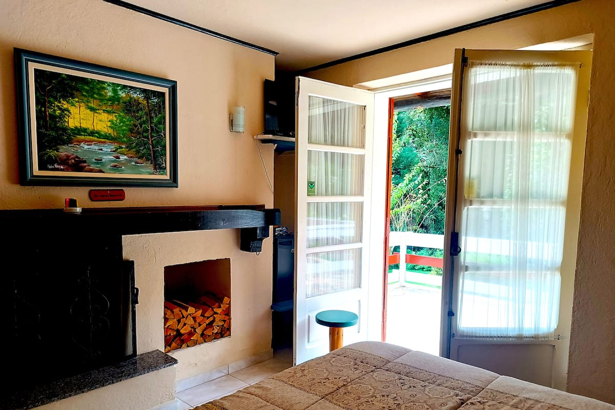 Quarto com lareira, um quadro e vista para o verde lá fora.