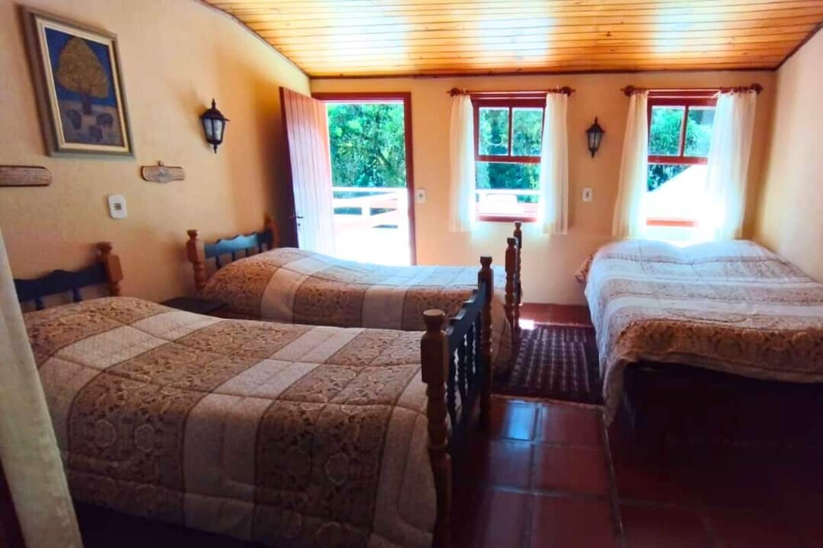 Quarto com duas camas, cabeceiras de madeira, teto de madeira e janelas com cortinas.