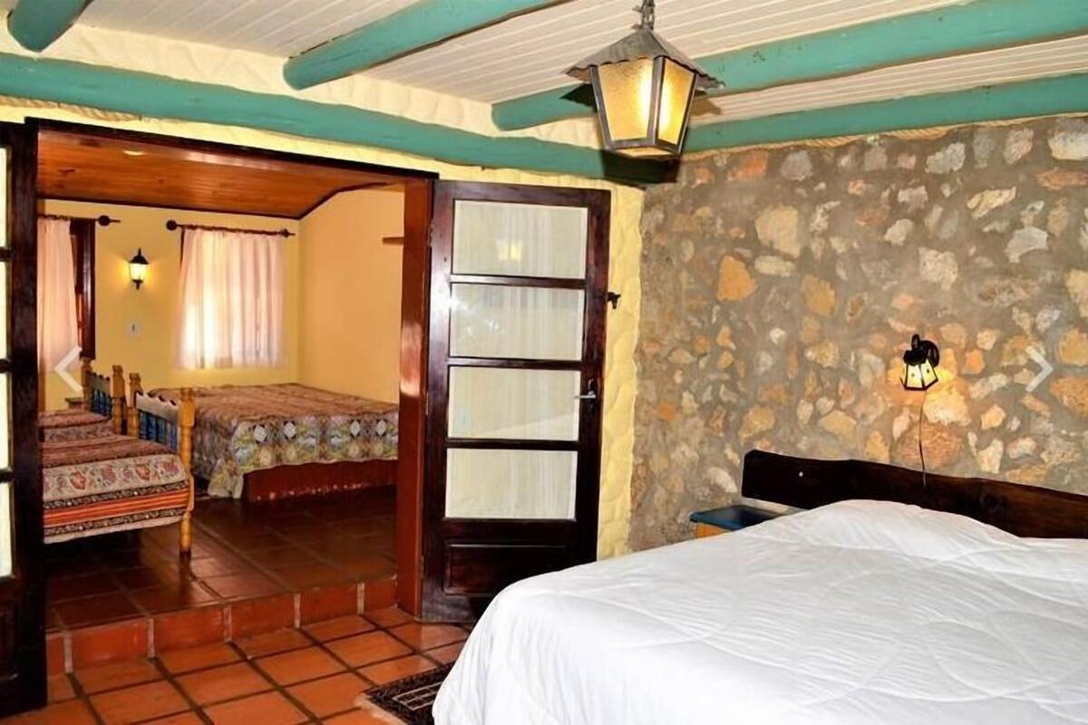 Quarto tradicional com cama, porta de madeira e parede de pedra.