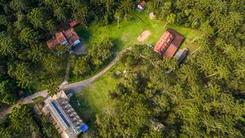Vista aérea de um bairro residencial com várias casas, um prédio grande com telhado azul e vegetação densa ao redor.