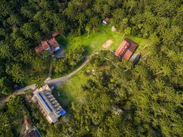 Vista aérea de um bairro residencial com várias casas, um prédio grande com telhado azul e vegetação densa ao redor.