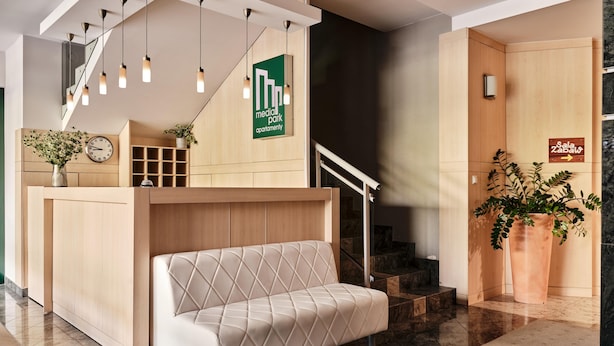Uma área de recepção moderna com um sofá, um relógio, uma placa com o nome 'Media Park Apartment' e uma escada.