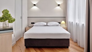 Quarto de hotel moderno com uma cama grande, mesas de cabeceira, abajur e um vaso com plantas verdes.