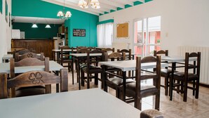 Uma sala de jantar com mesas e cadeiras de madeira, paredes verde-água e um candelabro.