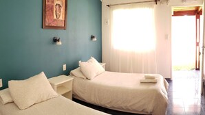 Quarto com duas camas, um quadro na parede e uma janela com cortinas.