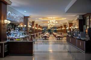 Um amplo hall de hotel com área de estar central, balcão de alimentos e um lustre moderno.