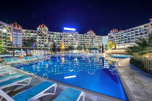 Um hotel com uma piscina grande, várias varandas e fachada bem iluminada.