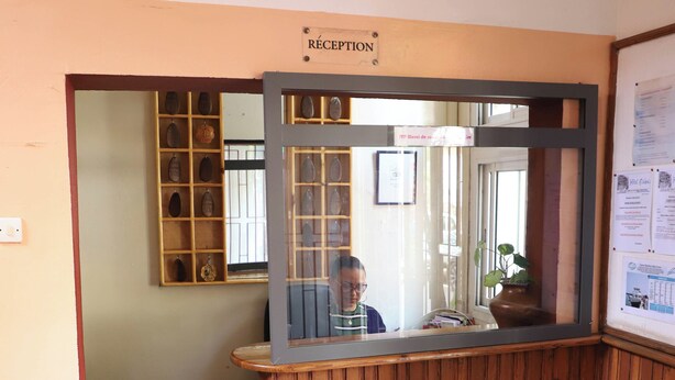 Uma área de recepção com uma mesa de madeira, um espelho, uma cadeira de madeira e a placa da recepção.