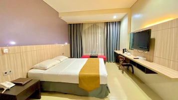 Quarto de hotel com cama, escrivaninha, televisão e minibar.