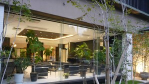 Interior de um hotel moderno com paredes de vidro, plantas em vasos e áreas de estar.