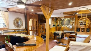 Quarto com escrivaninha de madeira, sofá branco, mesa de jantar e ventilador de teto.
