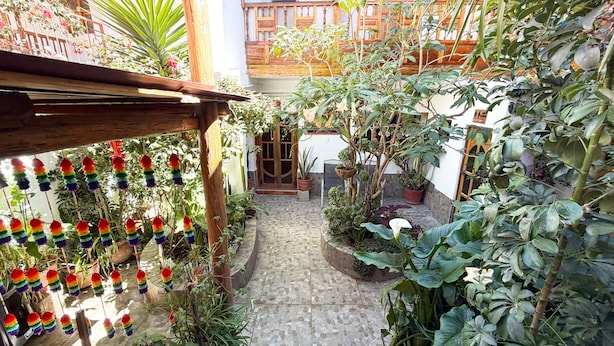 Um pátio com vasos de plantas, uma pérgula de madeira e piso de azulejos.