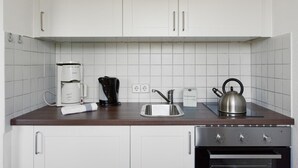 Uma cozinha com armários brancos, chaleira de aço inoxidável, cafeteira e forno.