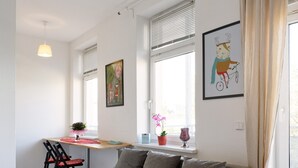 Uma sala de estar moderna com um sofá cinzento, uma mesa de jantar de madeira e uma área de cozinha ao fundo.
