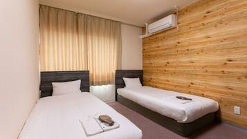 Quarto de hotel com duas camas, cortinas bege, painéis de madeira e ar condicionado.