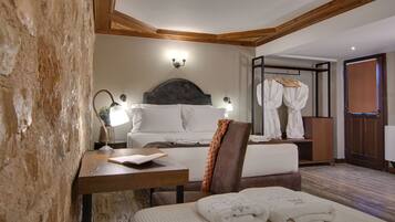 Quarto de hotel com duas camas, uma escrivaninha de madeira com abajur, uma cadeira e um suporte para roupões com roupões.