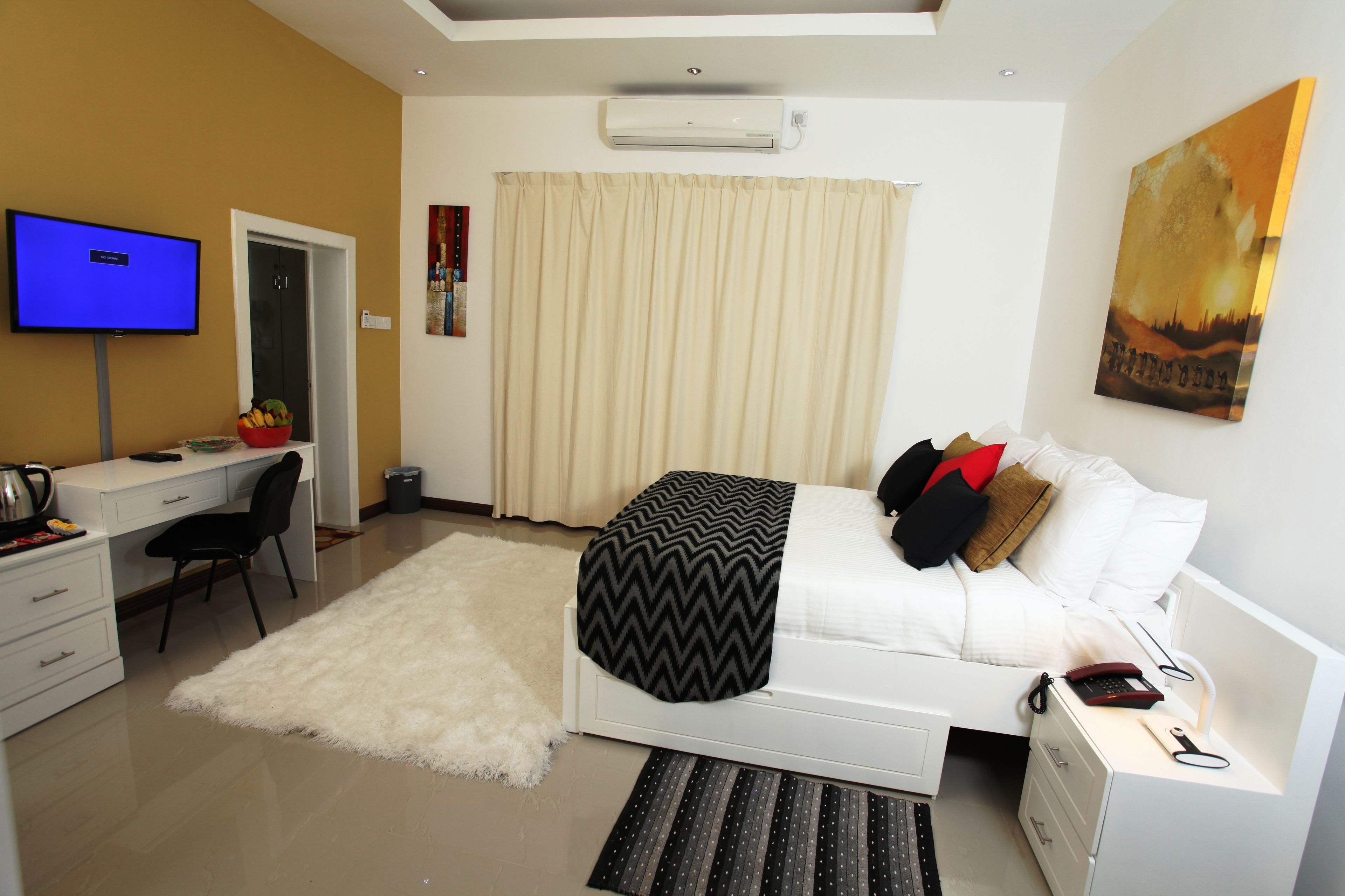 Quarto de hotel com cama, escrivaninha, cadeira, televisão e um quadro na parede.