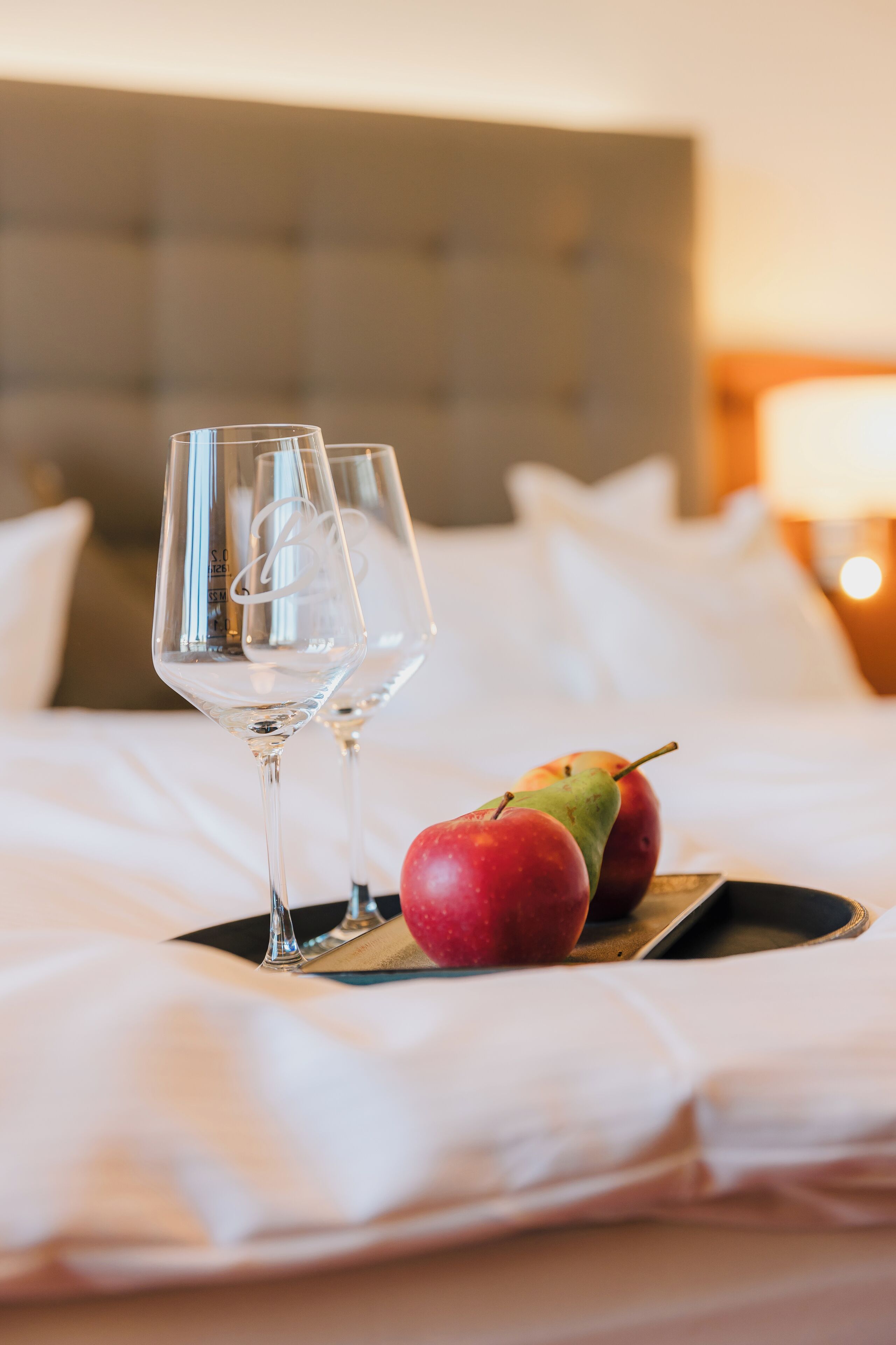 Uma bandeja com duas taças de vinho e duas maçãs sobre uma cama.