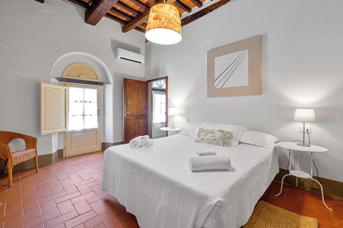Quarto com cama, mesas de cabeceira, uma cadeira e uma porta.