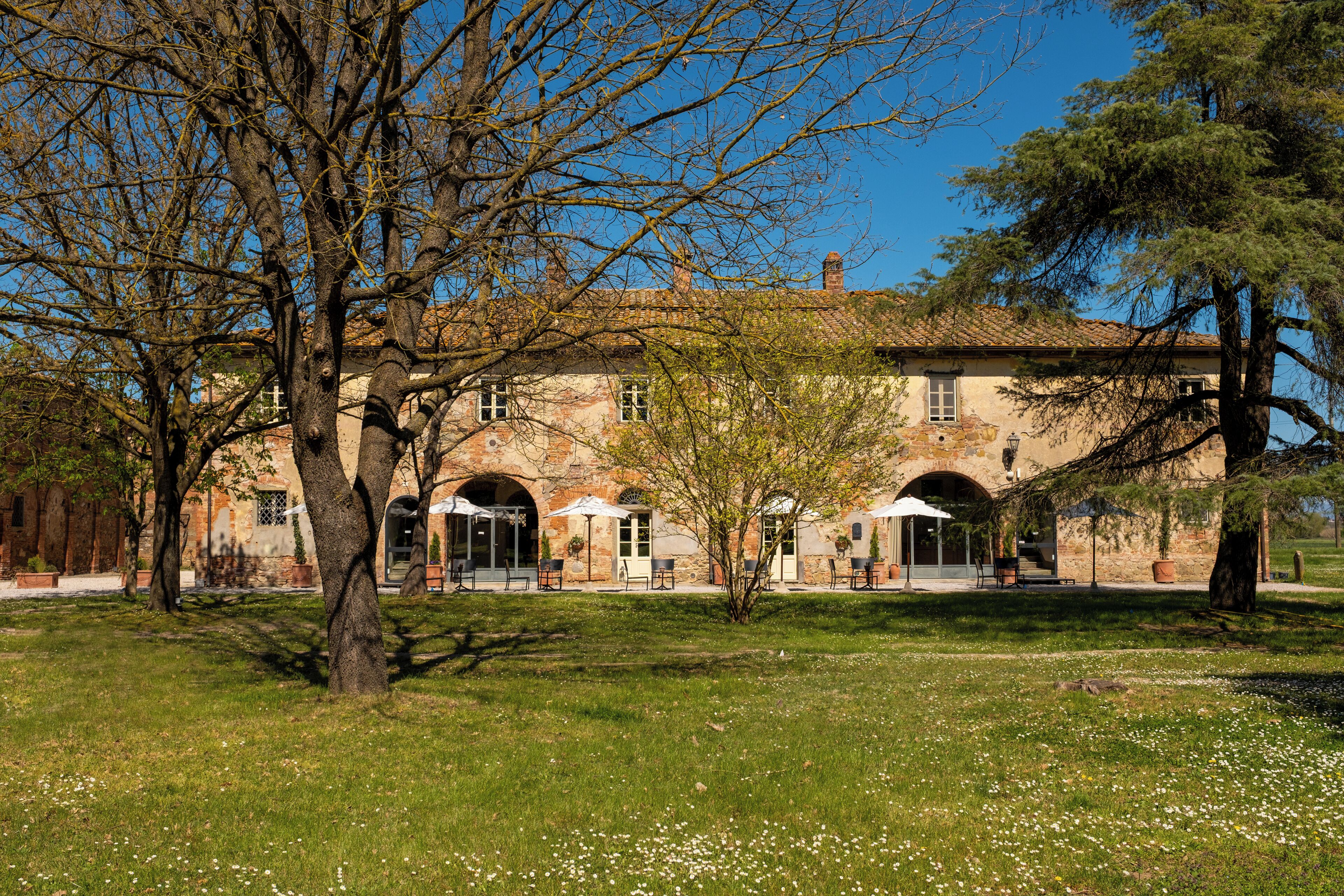 Um edifício de pedra com portais em arco, um pátio gramado e árvores.