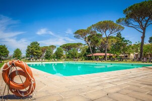 Piscina com boia, rodeada por árvores e mobiliário de exterior.