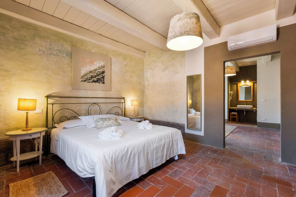 Quarto com cama, luminárias de cabeceira, um espelho e vista para o banheiro.