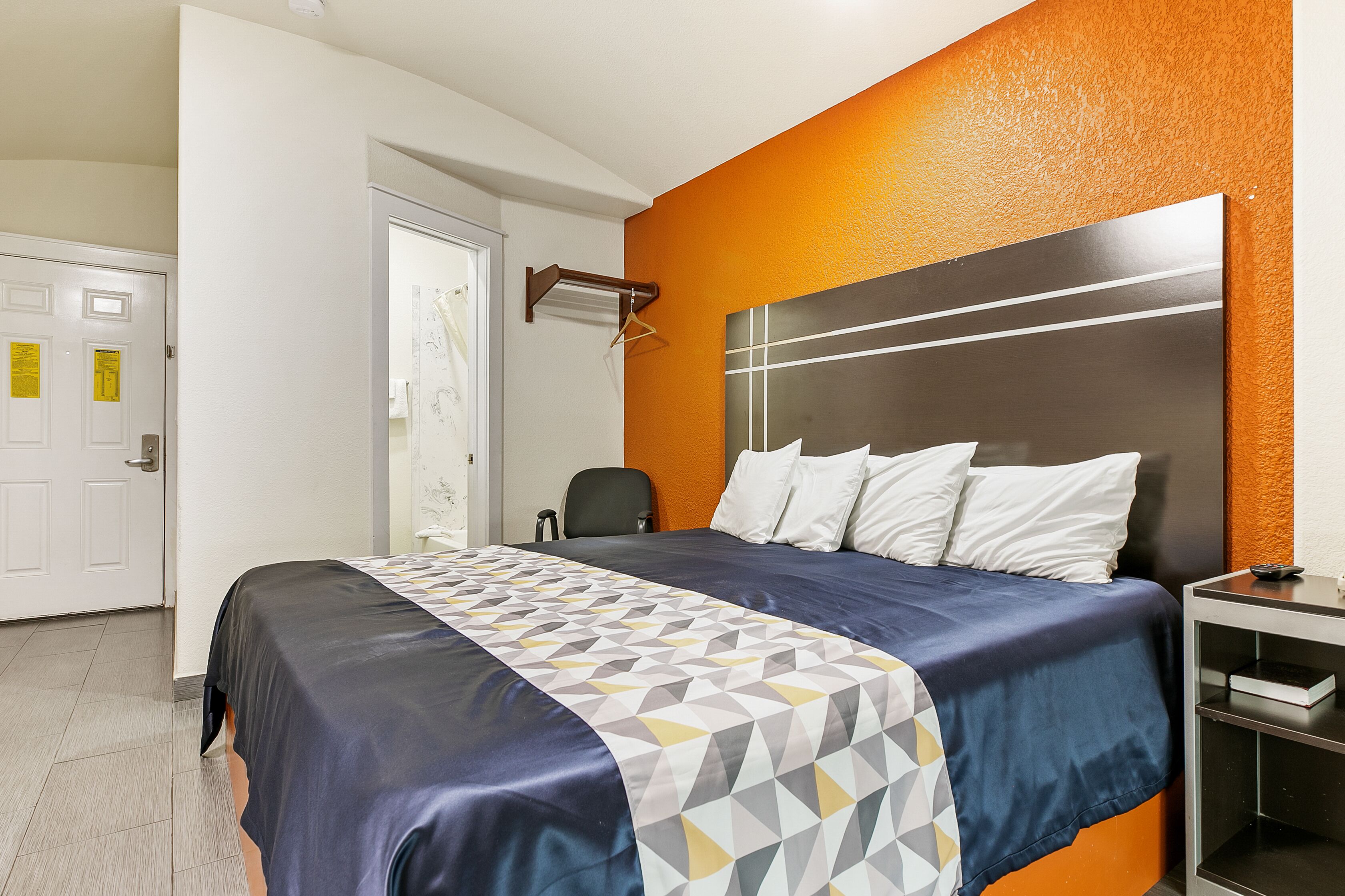 Quarto de hotel com uma cama, uma cadeira, uma mesa de cabeceira e uma porta.
