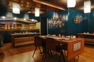 Interior de restaurante com mesas e cadeiras de madeira, um balcão e pratos decorativos na parede.