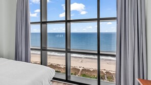 Quarto com uma grande janela que oferece vista para a praia e o oceano.