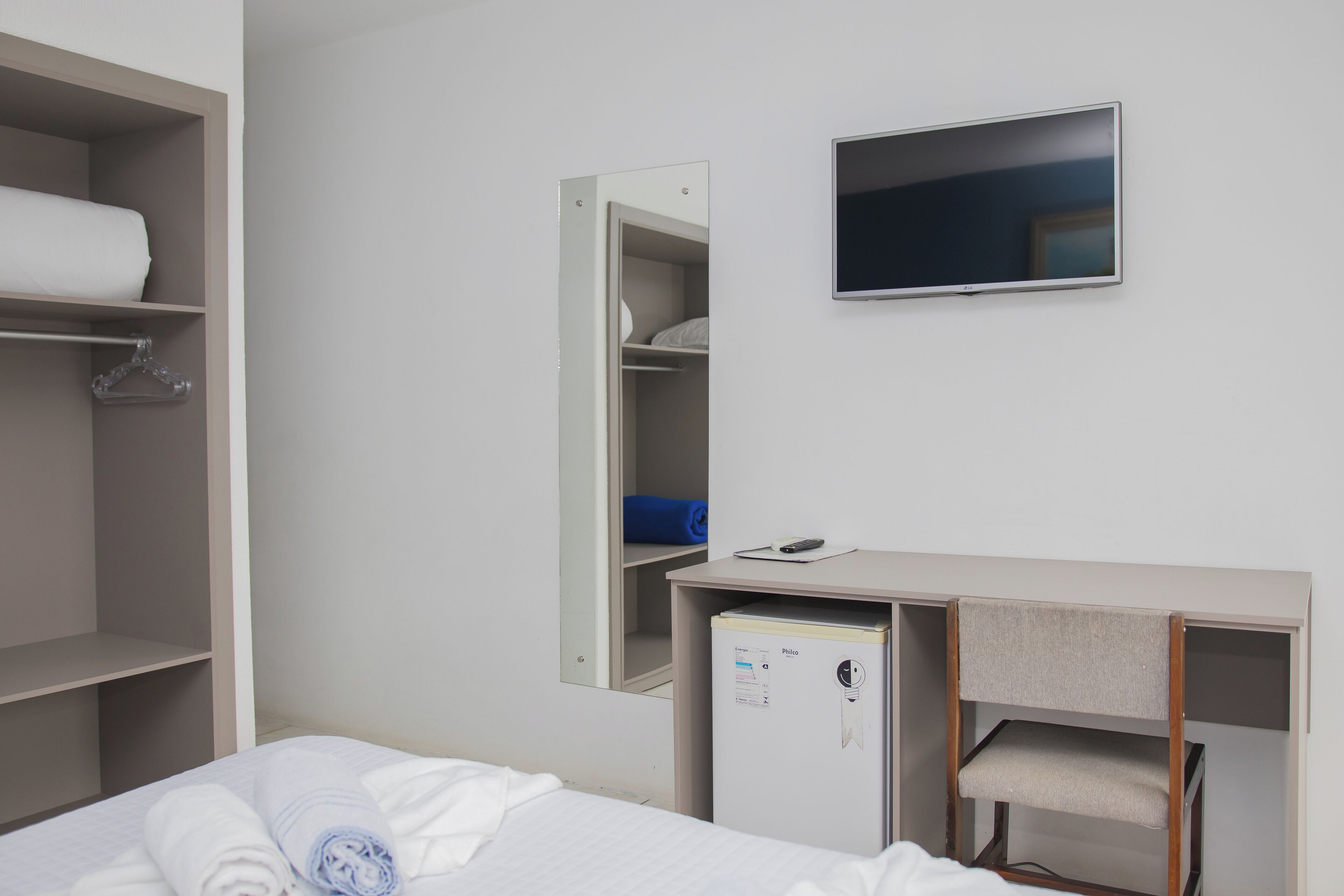 Quarto de hotel com cama, escrivaninha com computador, espelho e televisão.
