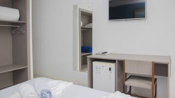 Quarto de hotel com cama, escrivaninha com computador, espelho e televisão.