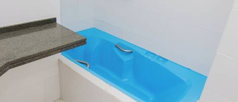 Casa de banho com banheira azul, azulejos brancos, bancada de granito e barra de apoio.