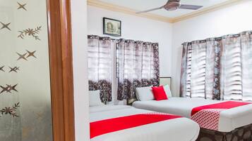Quarto de hotel com duas camas, um ventilador de teto e cortinas com padrão floral.