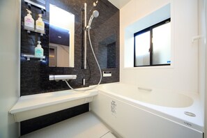 Uma casa de banho moderna com uma banheira grande, chuveiro embutido e toucador com prateleiras para artigos de higiene pessoal.