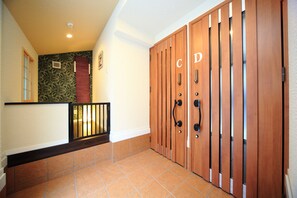 Um corredor com porta de madeira identificada por letras, chão de azulejos e escada com corrimão.