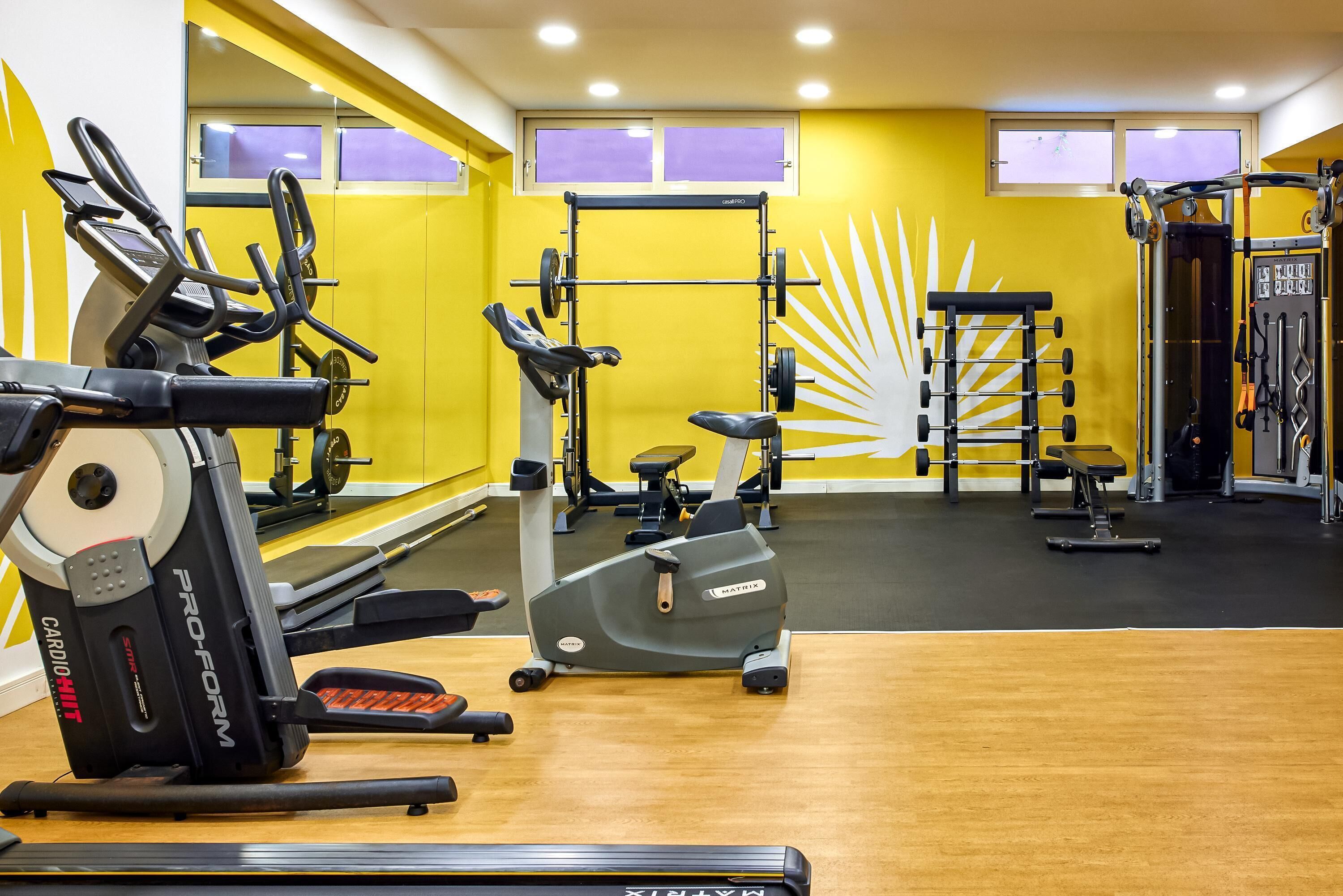 Uma academia com equipamentos de cardio, estações de musculação e espelhos.