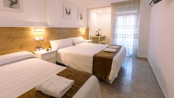 Quarto de hotel com duas camas, uma escrivaninha, uma cadeira e uma janela com cortinas.
