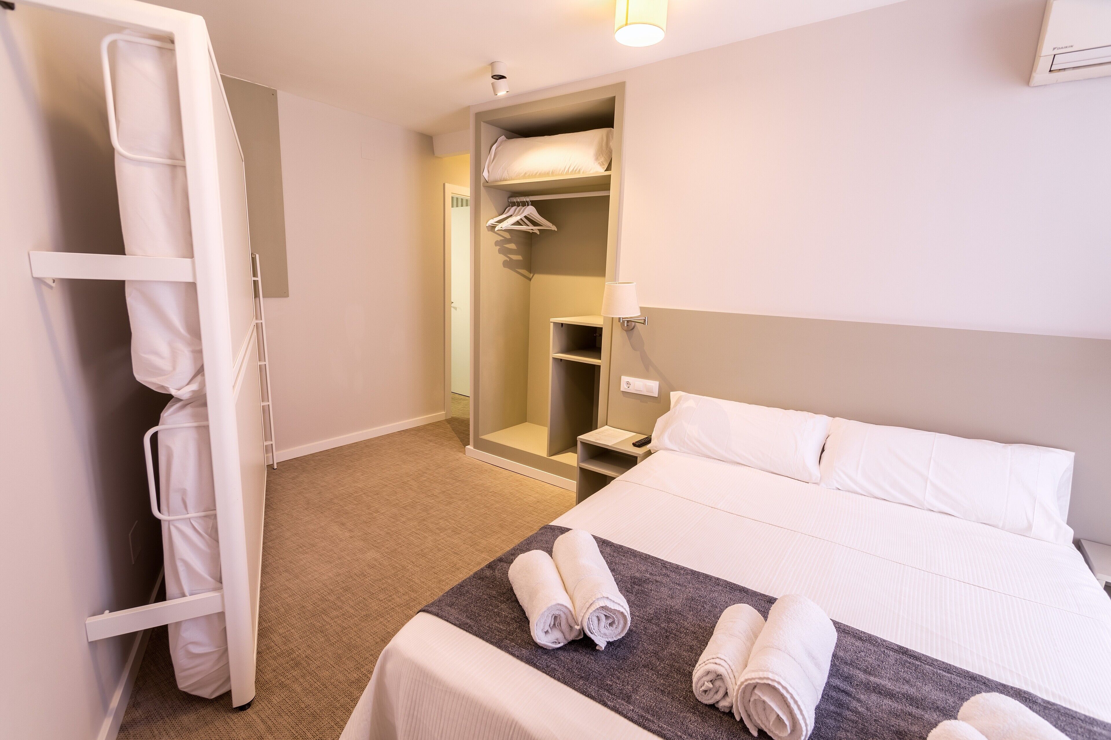 Quarto de hotel com cama, guarda-roupa, espelho e uma pequena mesa.